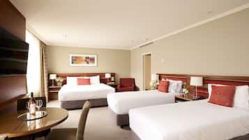 Quarto de hotel com duas camas, uma mesa de jantar e uma televisão.