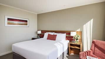 Quarto de hotel com uma cama grande, uma mesa de cabeceira de madeira, uma cadeira vermelha e um quadro na parede.