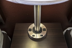 Uma luminária de mesa metálica com cúpula branca, base circular com duas tomadas elétricas e suporte metálico.