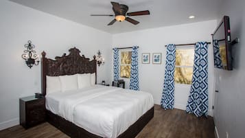 Quarto com uma cama grande, ventoinha no teto, mesa de cabeceira, televisão, cortinas estampadas e janela com vista.