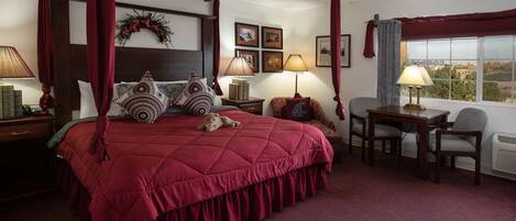 Uma cama de dossel com cortina e um edredom vermelho, um urso de pelúcia e vista para o campo pela janela.