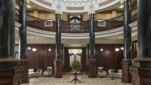 Um hall imponente com pé-direito alto, colunas de mármore e um arranjo floral central.
