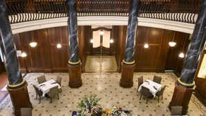 Um salão imponente com lustres elaborados, colunas de mármore e um arranjo floral central.