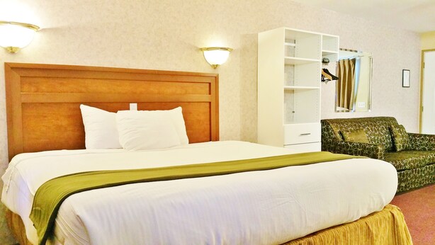Quarto de hotel com uma cama grande, um guarda-roupa, uma cadeira e um candeeiro fixado na parede.