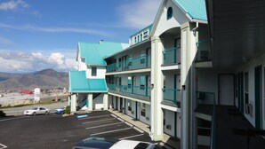 Um motel com telhado azul e paredes brancas, apresentando um estacionamento e um cenário montanhoso.
