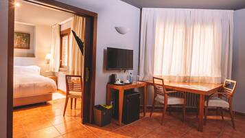 Quarto de hotel com cama, escrivaninha, televisão, cadeira e janela com cortinas.