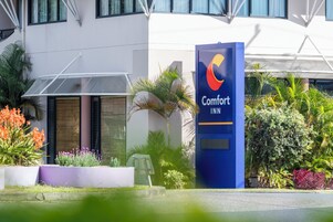 Um hotel Comfort Inn com uma placa azul grande, rodeado por vegetação exuberante e uma área de estar externa coberta.