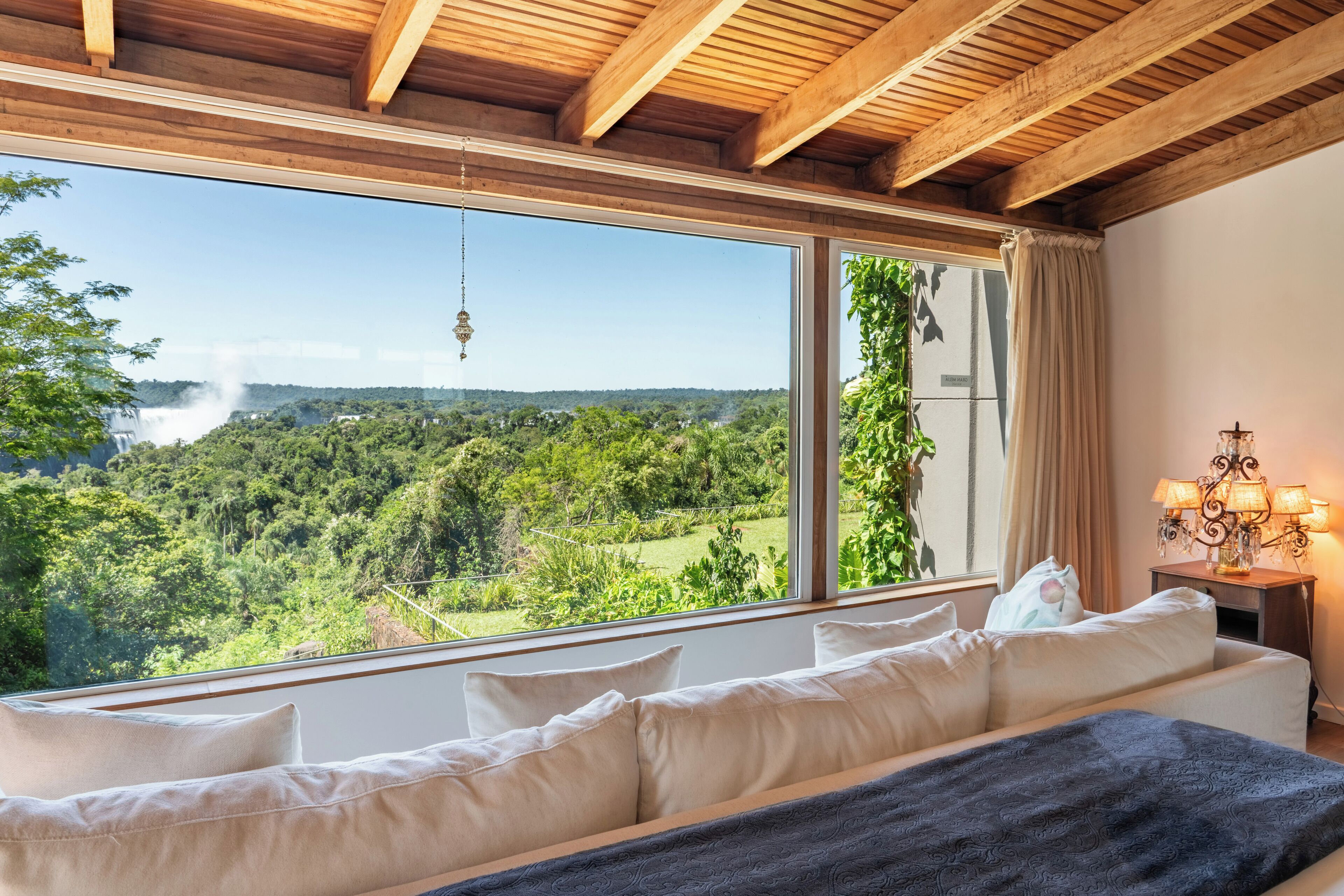 Quarto com uma janela grande que dá para uma paisagem verdejante e uma cachoeira.