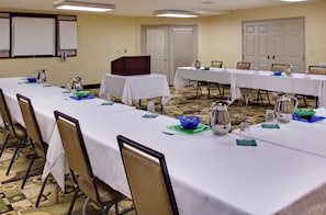 Sala de conferência com várias mesas, cadeiras e uma tela de projeção.