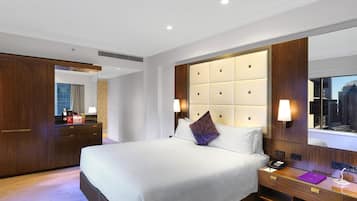Quarto de hotel com uma cama grande, um guarda-roupa de madeira, uma mesa de cabeceira com abajur e um espelho grande que reflete o quarto.