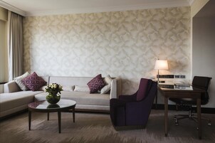 Quarto de hotel moderno com papel de parede estampado, um sofá, uma cadeira, uma escrivaninha e uma luminária.
