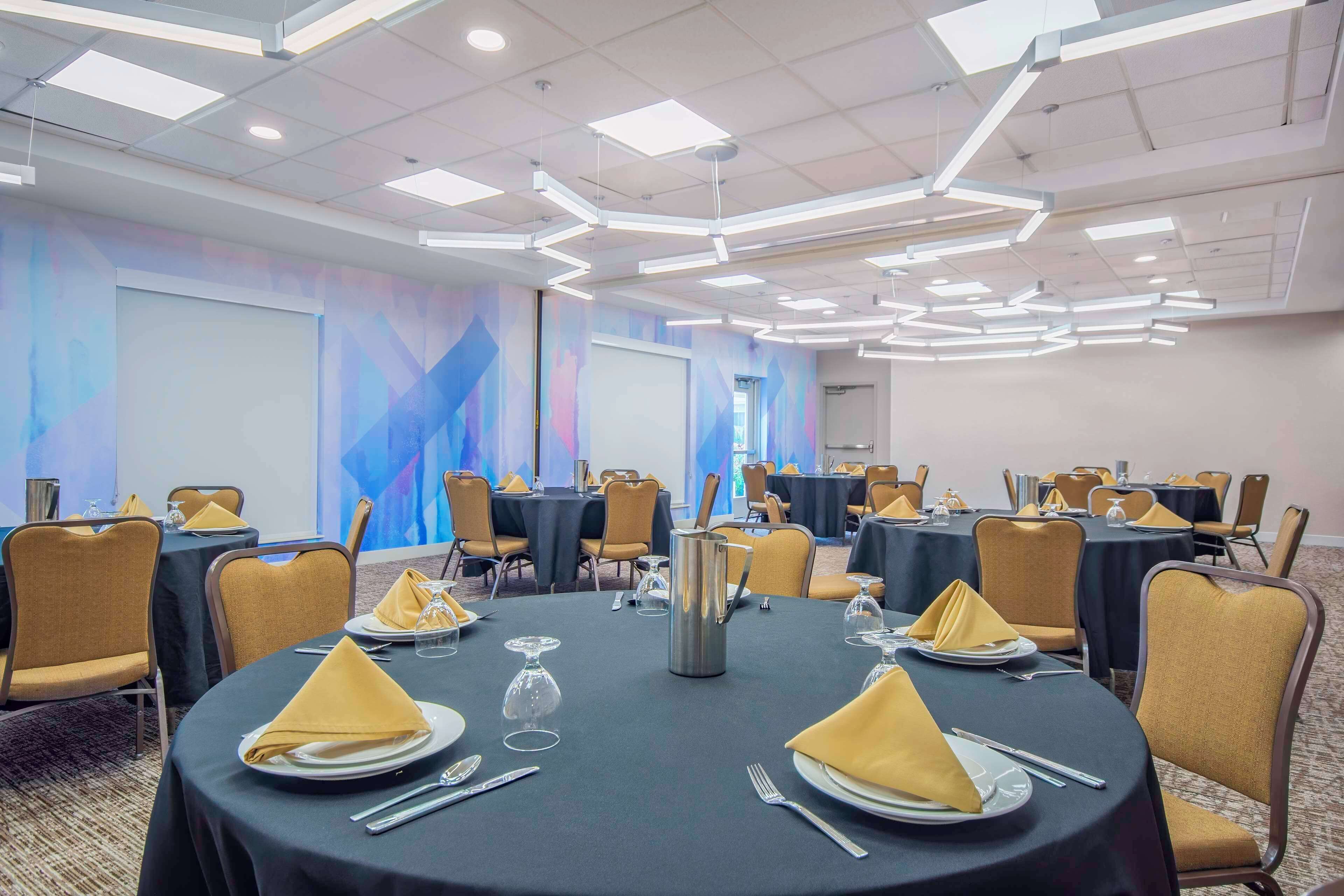 Uma sala de conferências com mesas redondas, cadeiras e uma tela de projeção.
