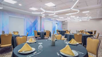 Uma sala de conferências com mesas redondas, cadeiras e uma tela de projeção.