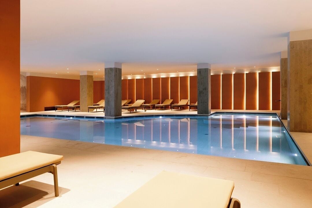 Piscina interior moderna com espreguiçadeiras e um solário.