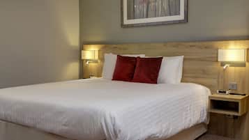 Cama bem arrumada com travesseiros brancos e vermelhos, cabeceira de madeira e abajures laterais.