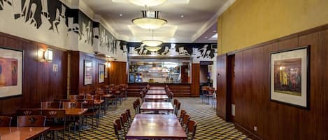 Restaurante com várias mesas e cadeiras, piso estampado e obras de arte nas paredes.