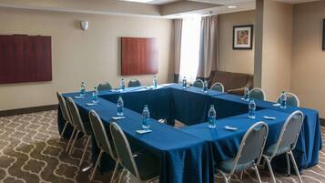 Uma sala de conferência com uma mesa comprida, cadeiras, garrafas de água e piso coberto por carpete.