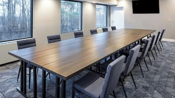 Uma sala de conferências com uma mesa comprida, cadeiras, janelas amplas e uma televisão de tela plana.