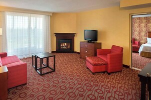 Quarto de hotel com lareira, televisão, sofá vermelho e tapete estampado.