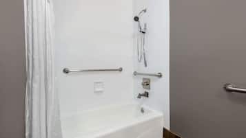 Casa de banho com banheira branca, chuveiro com chuveiro manual e barras de apoio.