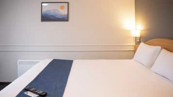 Quarto de hotel com cama, controle remoto, quadro pendurado na parede e luminária fixada na parede.