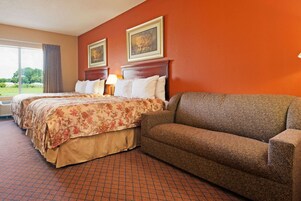 Quarto de hotel com duas camas, um sofá e uma janela grande com vista para áreas verdes.