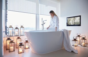 Um banheiro moderno com uma banheira independente, uma janela ampla e várias velas acesas.