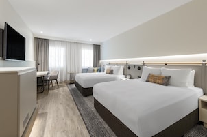 Quarto de hotel com duas camas, uma escrivaninha e uma televisão.
