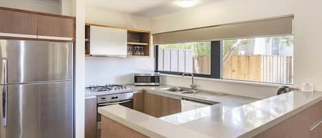 Uma cozinha moderna com eletrodomésticos de aço inoxidável, micro-ondas embutido e uma grande ilha com pia.