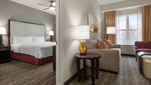 Quarto de hotel com uma cama, um sofá, uma mesinha e uma janela com cortinas.