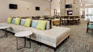 Um amplo hall de hotel com um sofá comprido, várias mesas e uma lareira.