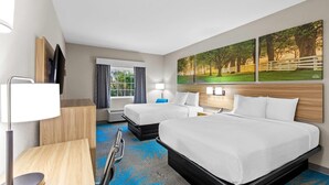 Quarto de hotel com duas camas, uma escrivaninha, uma cadeira, uma televisão e uma janela grande.