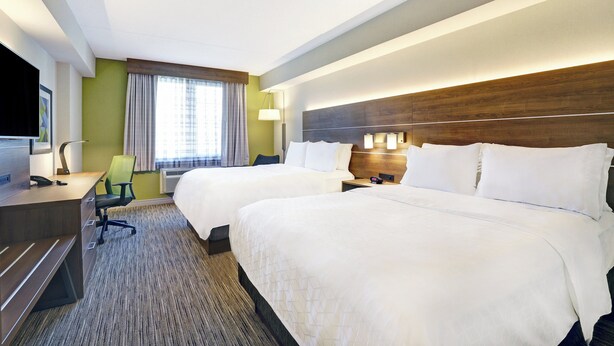Quarto de hotel com duas camas, uma escrivaninha, uma cadeira, televisão e janela com cortinas.