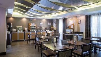 Uma sala de jantar de hotel com várias mesas e cadeiras, uma área de cozinha e um balcão de café da manhã.