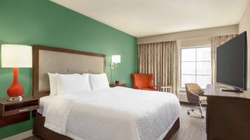 Quarto de hotel com uma cama grande, uma escrivaninha, uma televisão e uma cadeira.