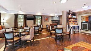 Um lobby de hotel com área de refeições, lareira, televisão e bar de petiscos.