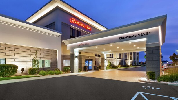 Entrada de um hotel Hampton Inn, com placa de via livre, arquitetura moderna e sinal de boas-vindas.