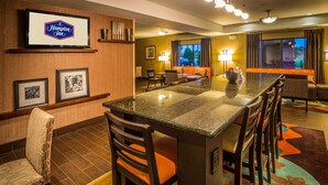 Quarto de hotel Hampton Inn com uma grande mesa ilha, cadeiras estilo bar, um sofá e uma mesa de jantar.