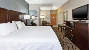 Quarto de hotel com uma cama grande, uma escrivaninha com televisão de tela plana, uma cadeira, um abajur e um guarda-roupa.