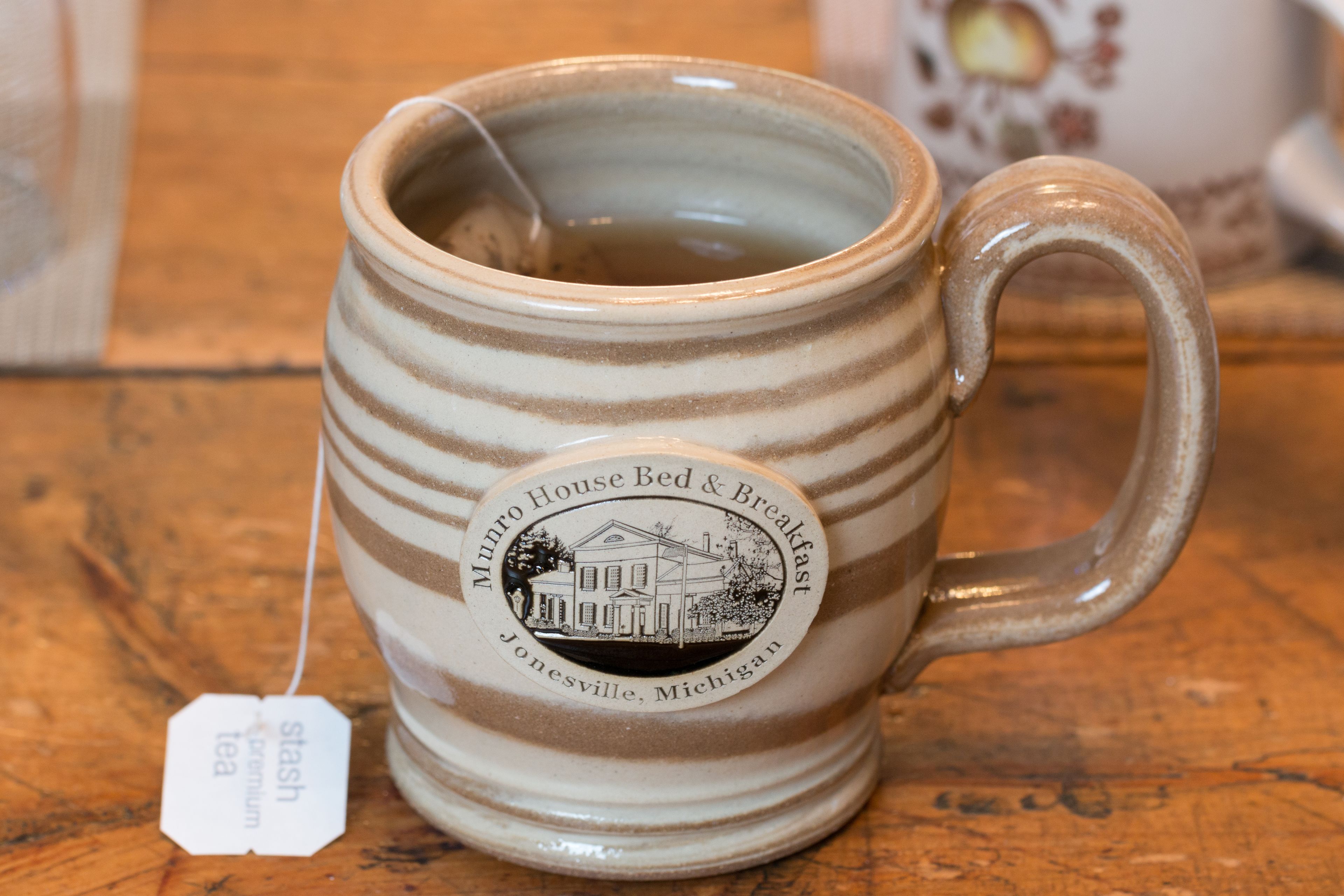 Uma caneca de cerâmica com alça, um sachê de chá e uma etiqueta com a inscrição "Munro House Bed & Breakfast, Jonesville, Michigan".