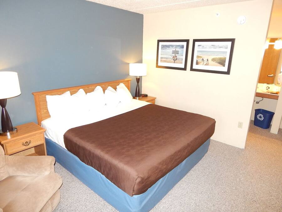 Quarto de hotel com cama, mesa de cabeceira, abajur e duas imagens emolduradas na parede.