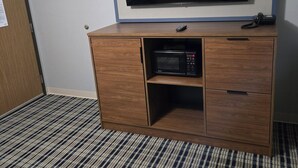 Quarto de hotel com uma televisão de tela plana grande fixada na parede, um armário de madeira com micro-ondas e um tapete listrado.