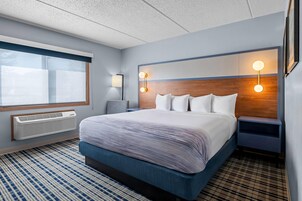 Quarto de hotel com cama grande, mesas de cabeceira, janela e luminária fixada na parede.
