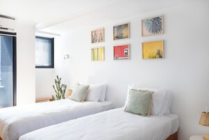 Quarto de hotel com duas camas, uma janela e quatro quadros na parede.