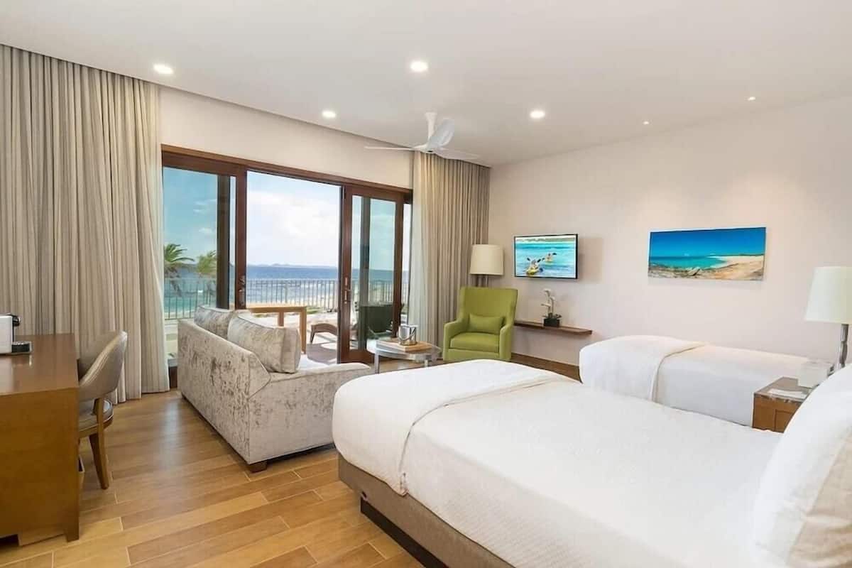 Quarto de hotel com cama, sofá, escrivaninha, cadeira, televisão e um quadro.