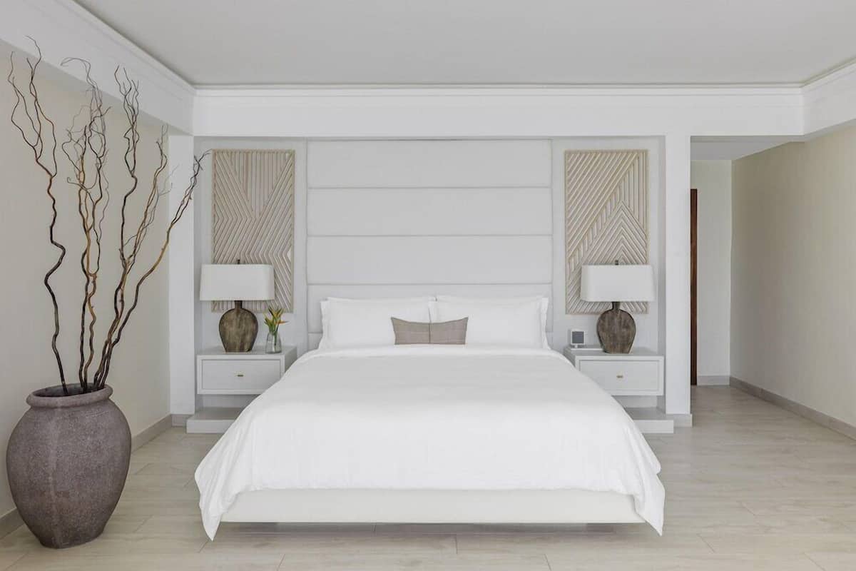 Quarto moderno com uma cama grande, duas mesas de cabeceira, um criado-mudo e um vaso decorativo.