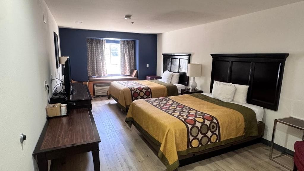Quarto de hotel com duas camas, uma escrivaninha, uma cadeira, uma televisão e uma janela com cortinas.