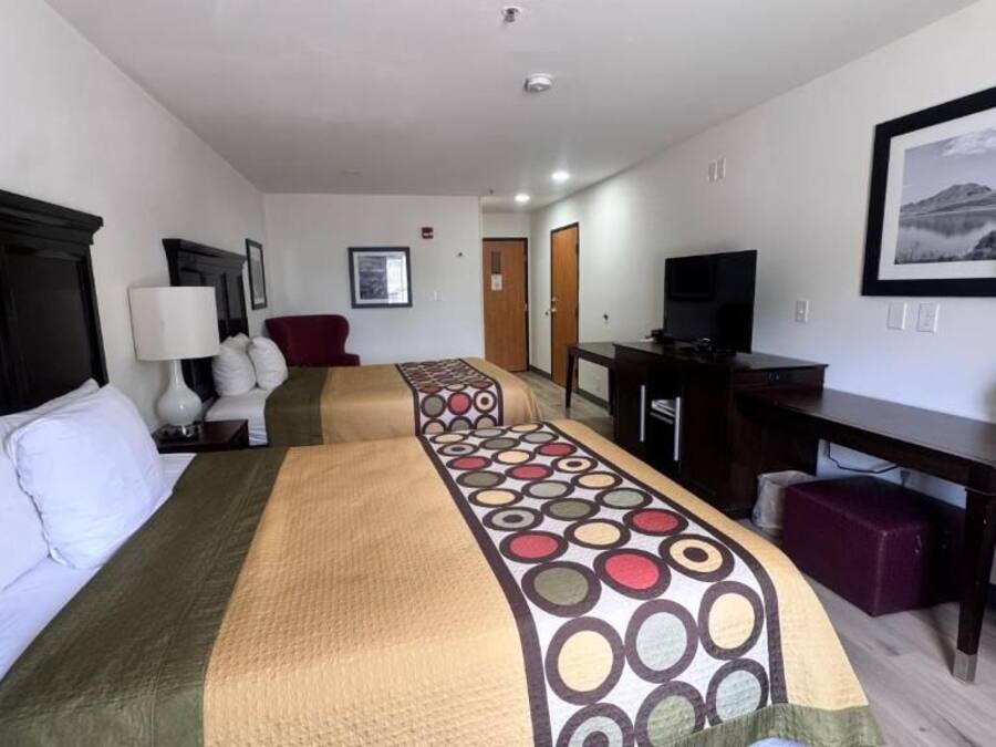Quarto de hotel com cama, escrivaninha, cadeira, televisão e um quadro na parede.
