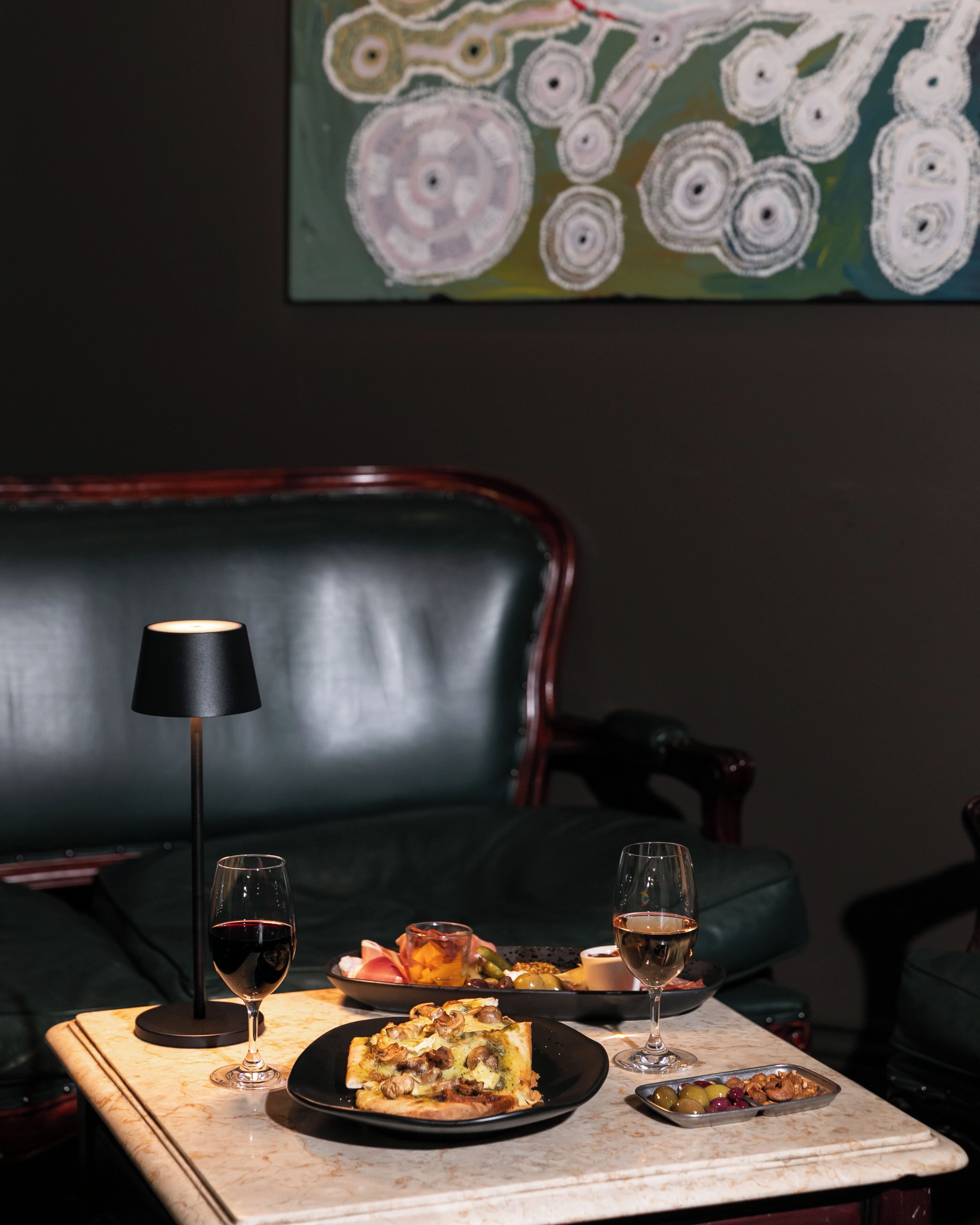 Uma mesa de jantar com pizza, dois copos de vinho e um abajur.