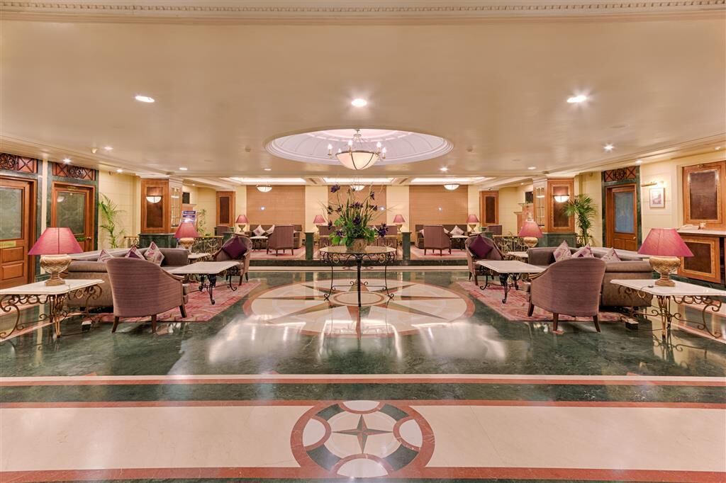 Um hall amplo com arranjo floral central, várias áreas de estar e piso de mármore polido.